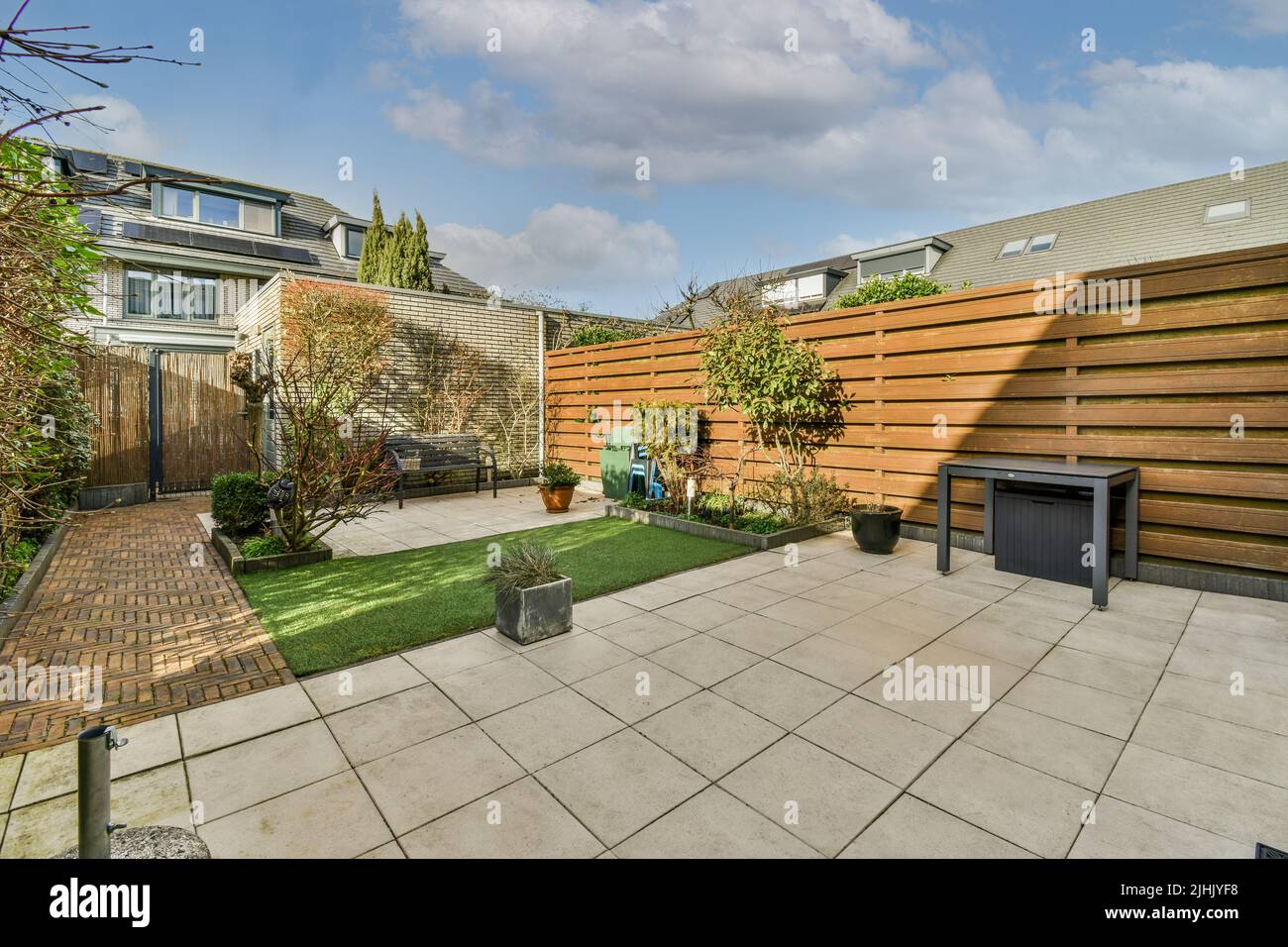 Neat paved patio with sitting area and small garden near wooden fence ...