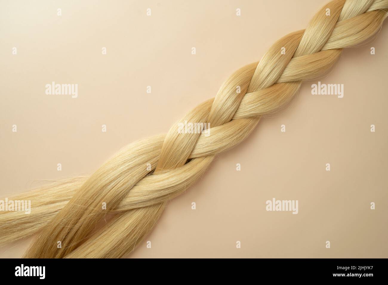 Woman's long blonde hair in the form of the tress lying on a beige ...