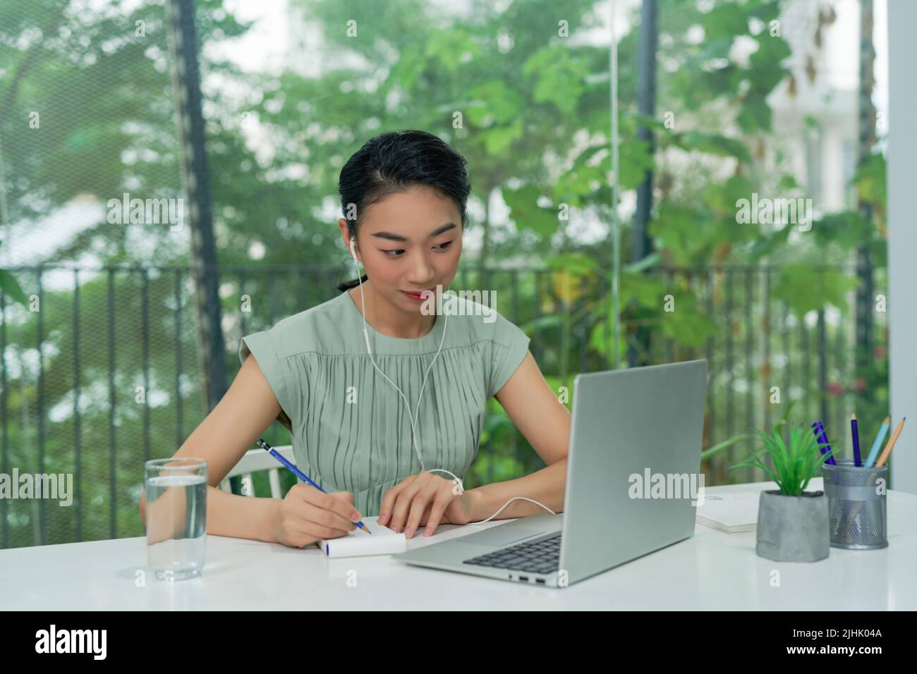 attractive cheerful young business woman write notebook look computer ...