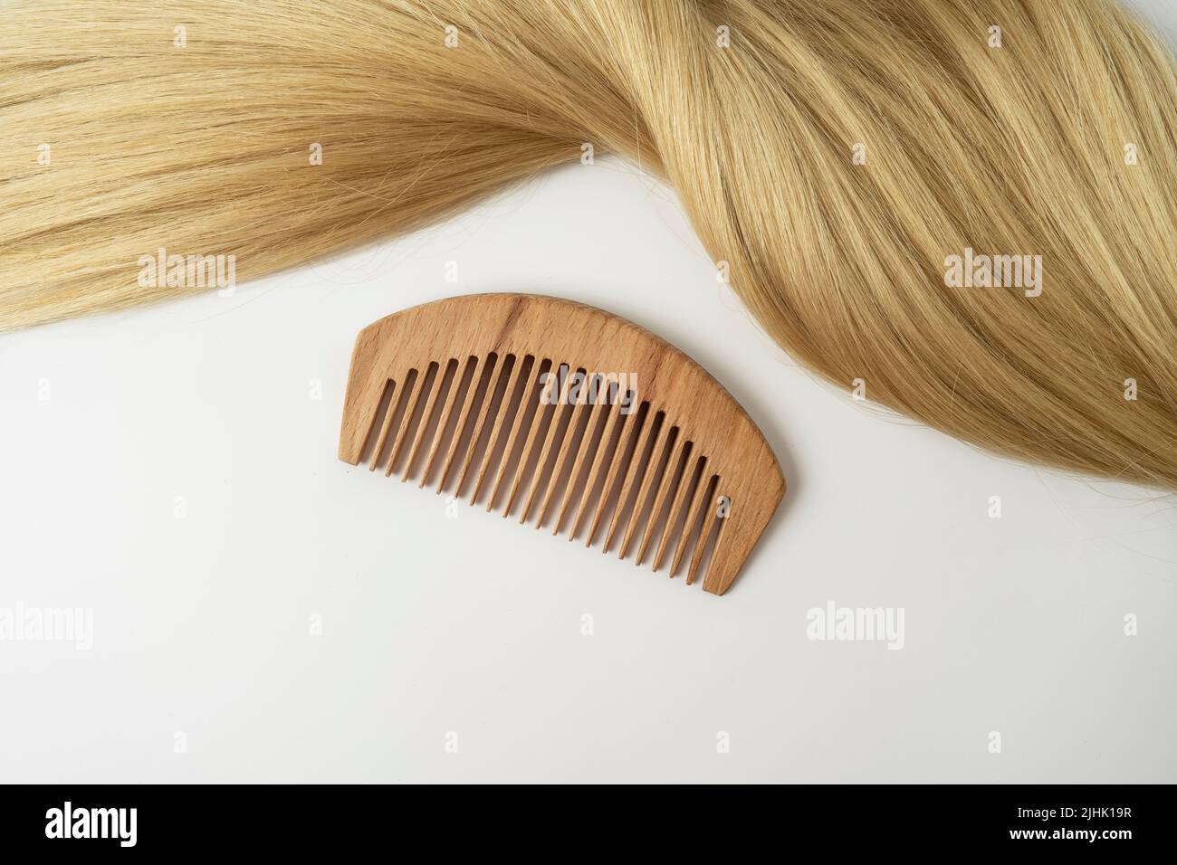A strand of blonde hair with a wooden comb on it lying on a white ...