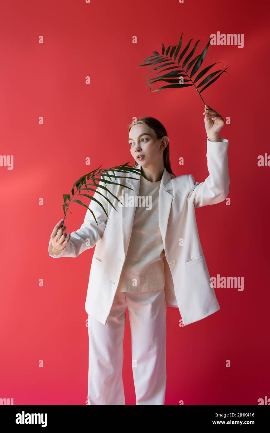 young woman in white clothes posing with green tropical leaves on ...