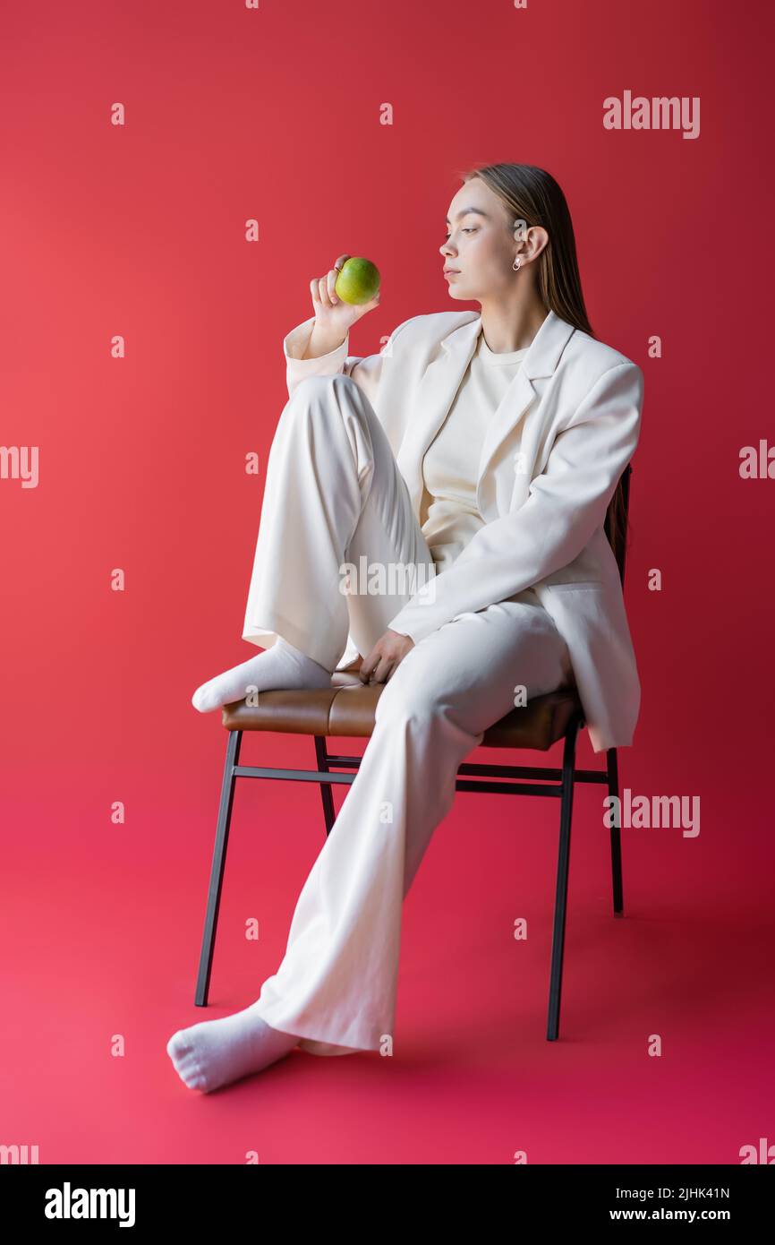 full length of woman in white suit and socks sitting on chair with ...
