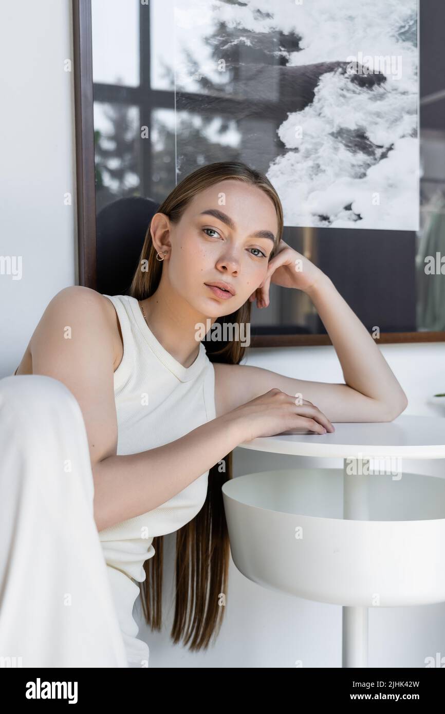 pretty woman leaning on coffee table near window and looking at camera ...