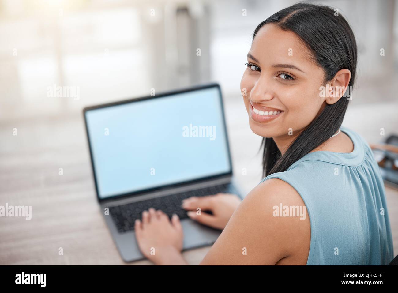 Smiling young businesswoman typing on her laptop keyboard, looking over ...