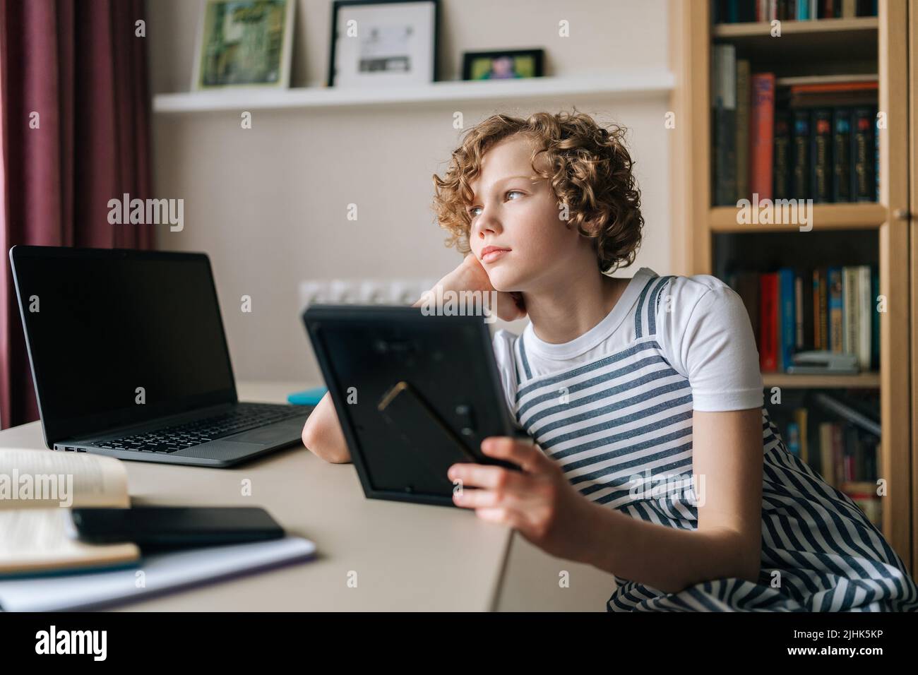Missed preteen girl holding photo frame with family portrait in hands ...