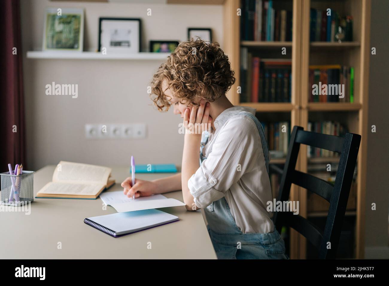 Side view of Caucasian little child schoolgirl writing to notebook with ...