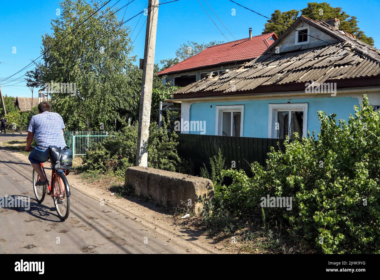 DACHNE, UKRAINE - JULY 19, 2022 - A man rides a bicycle past a house ...