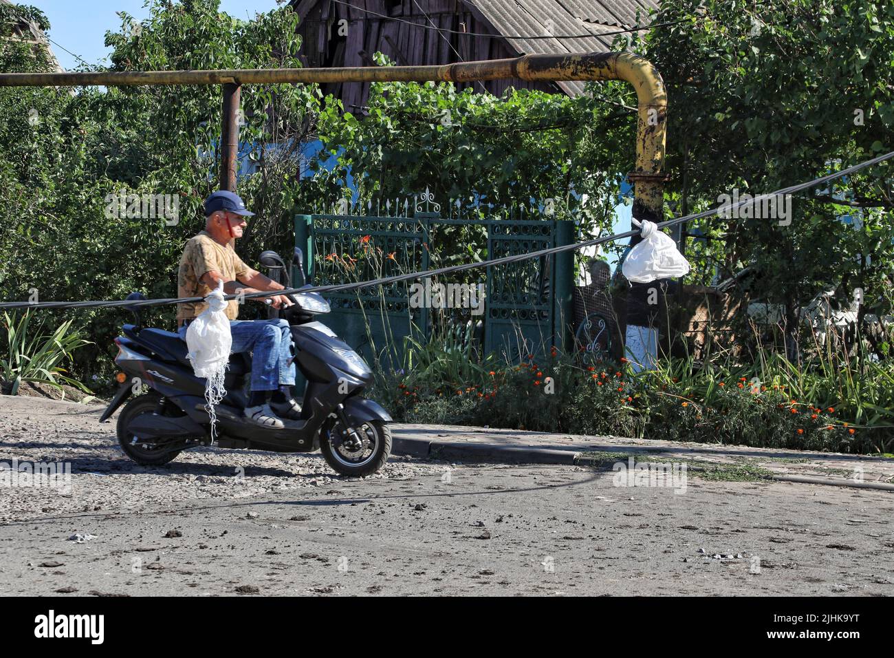 DACHNE, UKRAINE - JULY 19, 2022 - A senior man rides a scooter past a ...