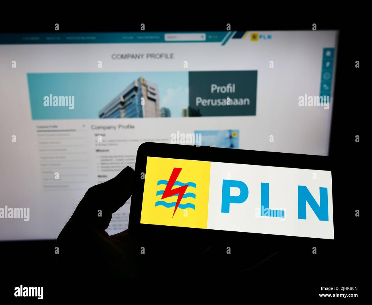 Person holding smartphone with logo of company PT Perusahaan Listrik ...