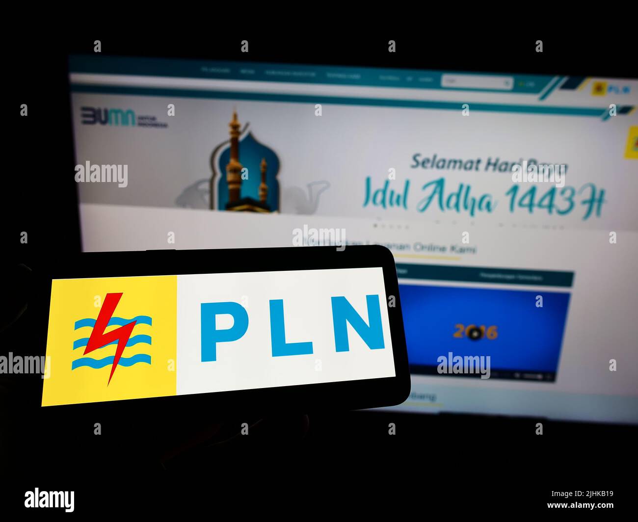 Person holding mobile phone with logo of company PT Perusahaan Listrik ...