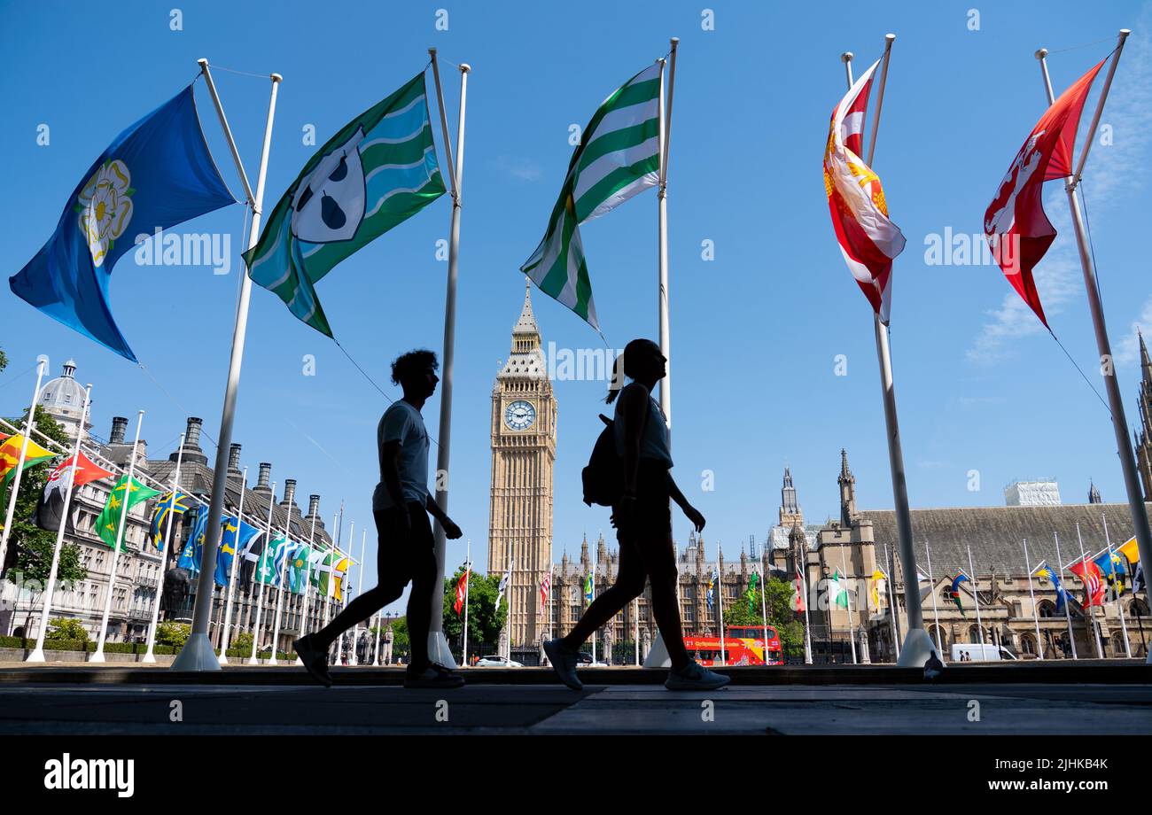 People walk in the shade past national flags in Parliament Square ...