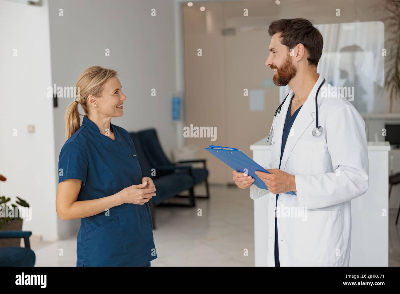 Two doctor colleagues talking during break standing in clinic hall ...