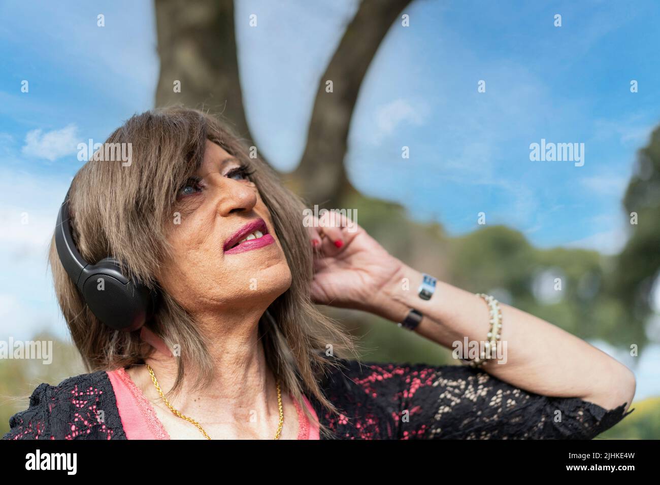 Trans woman listening to music outdoors with headphones. Expression of ...