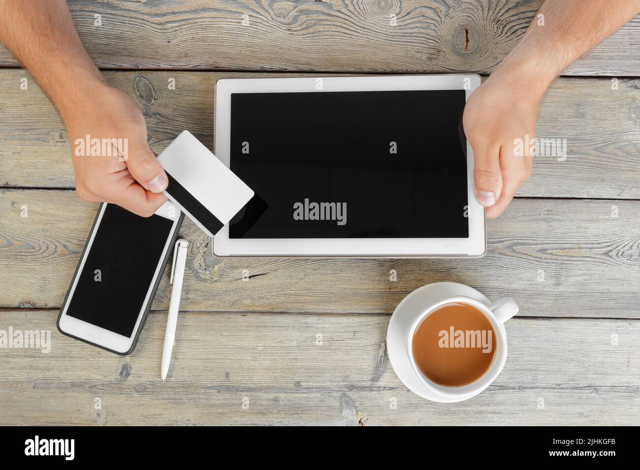 hands of a man holding tablet device over a wooden workspace table ...