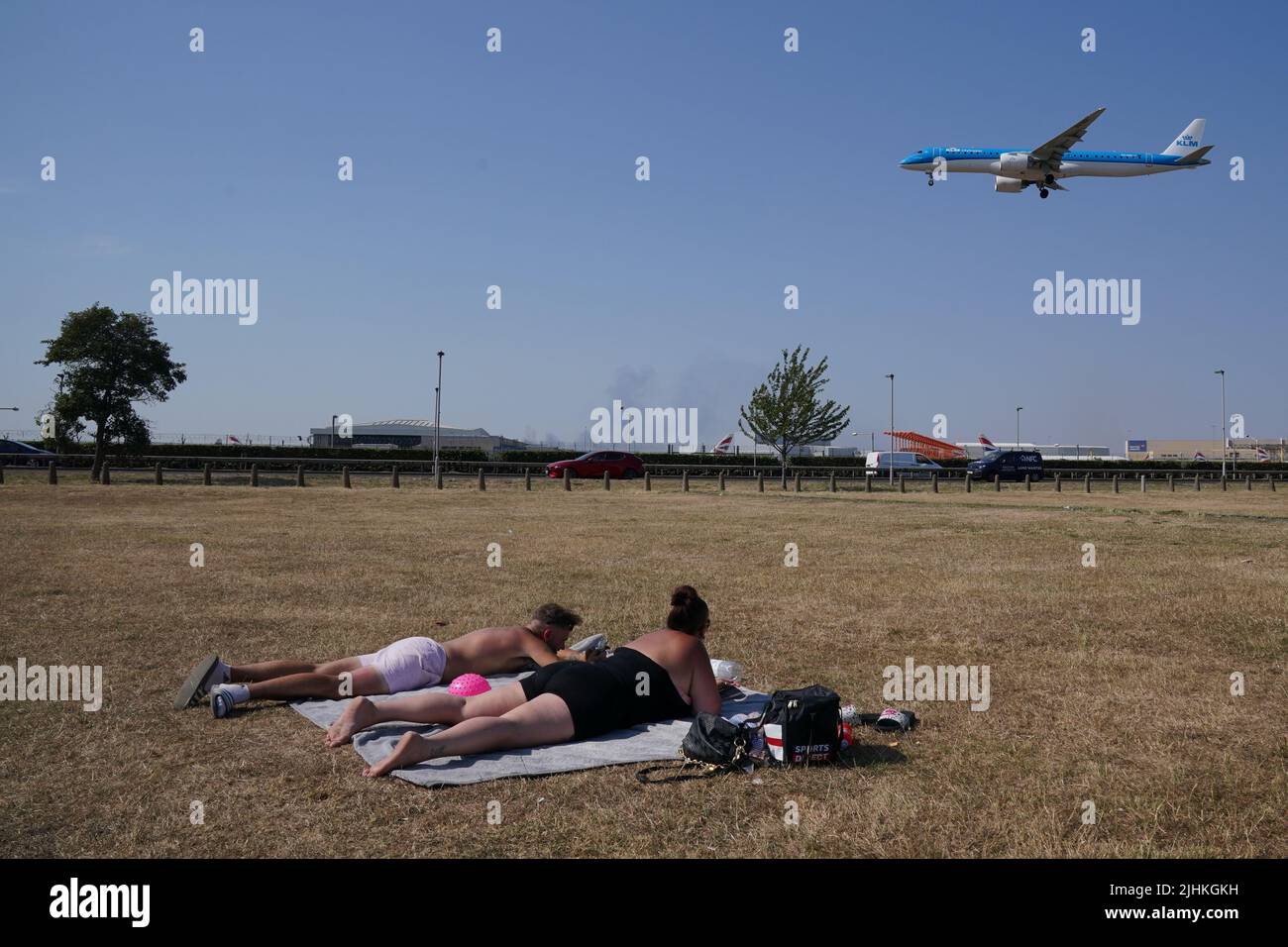 A couple sunbathe as a KLM flight comes into land at Heathrow Airport ...