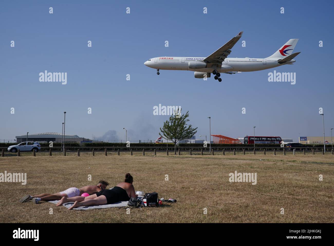 A couple sunbathe as a China Eastern flight comes into land at Heathrow ...