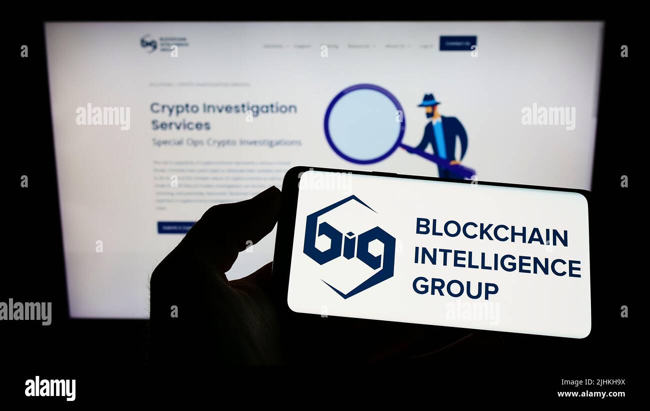 Person holding mobile phone with logo of company Blockchain Intelligence Group (BIG) on screen ...
