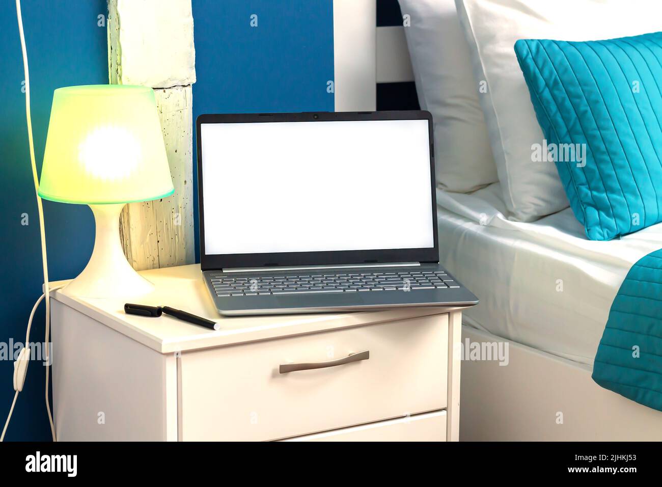 Open laptop computer with blank white screen next to lamp on bedside ...