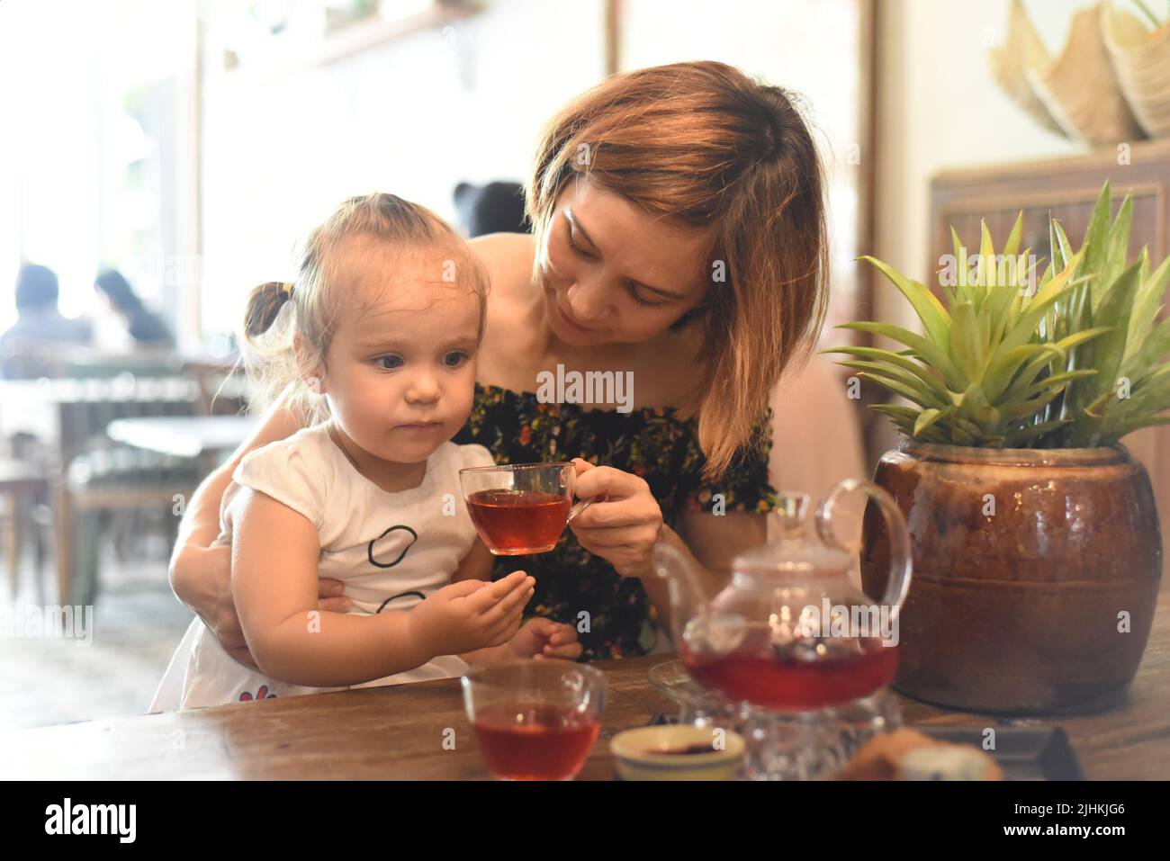 Young woman with a baby girl drinking tea from a tea pot in a coffee ...