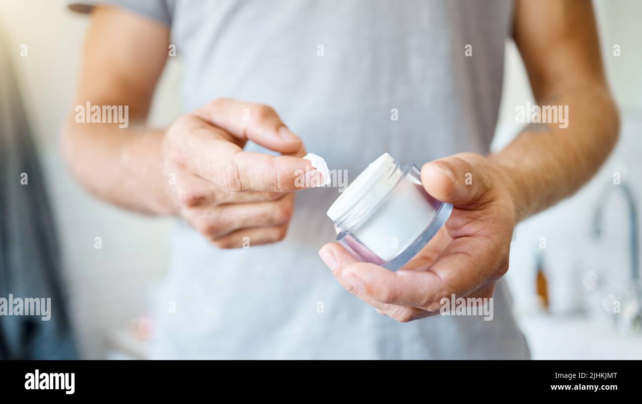 An unknown man applying cream or moisturiser to his face in a bathroom ...