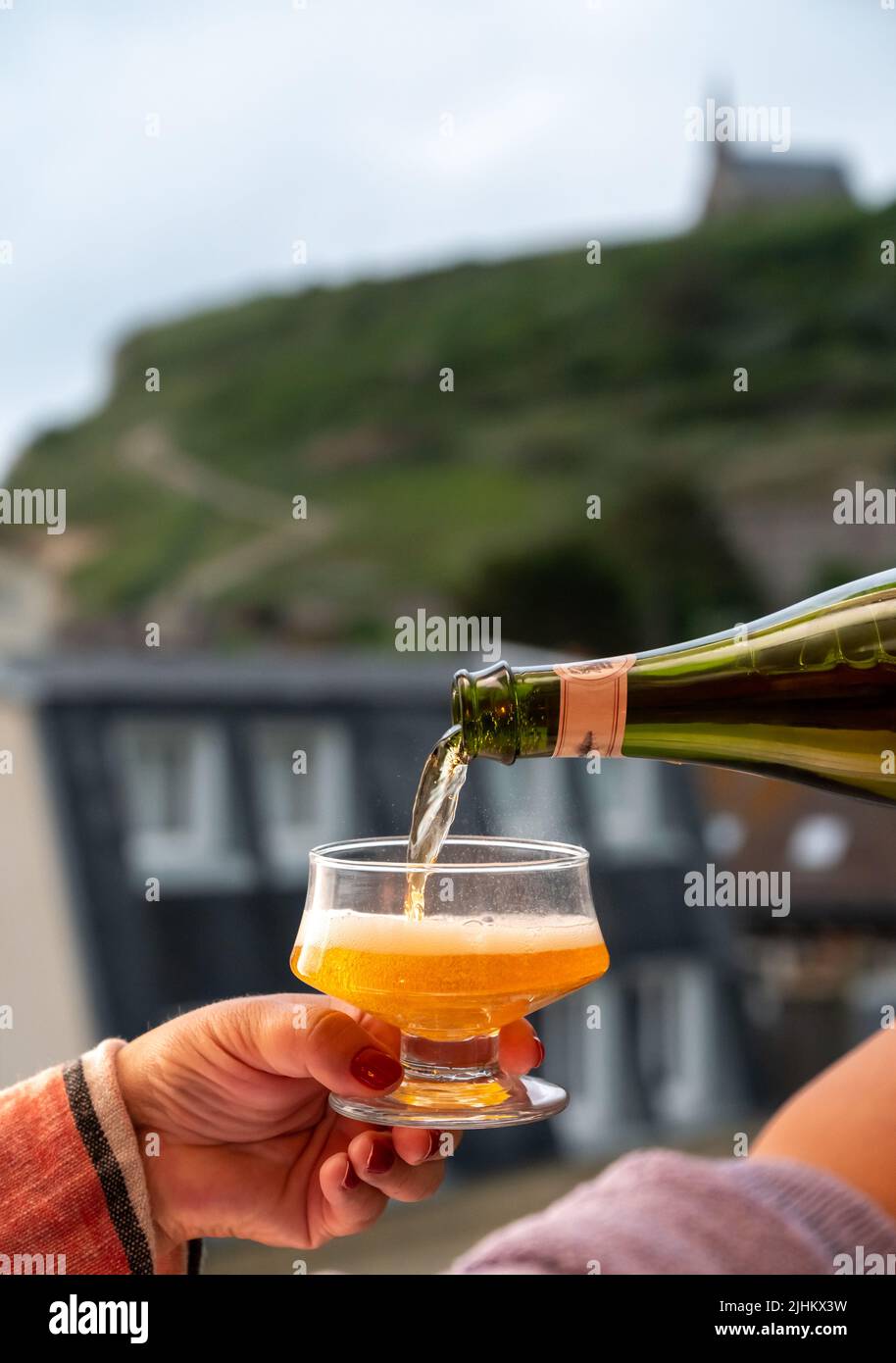 Pouring of tasty apple cider drink in glass with houses of Etretat ...