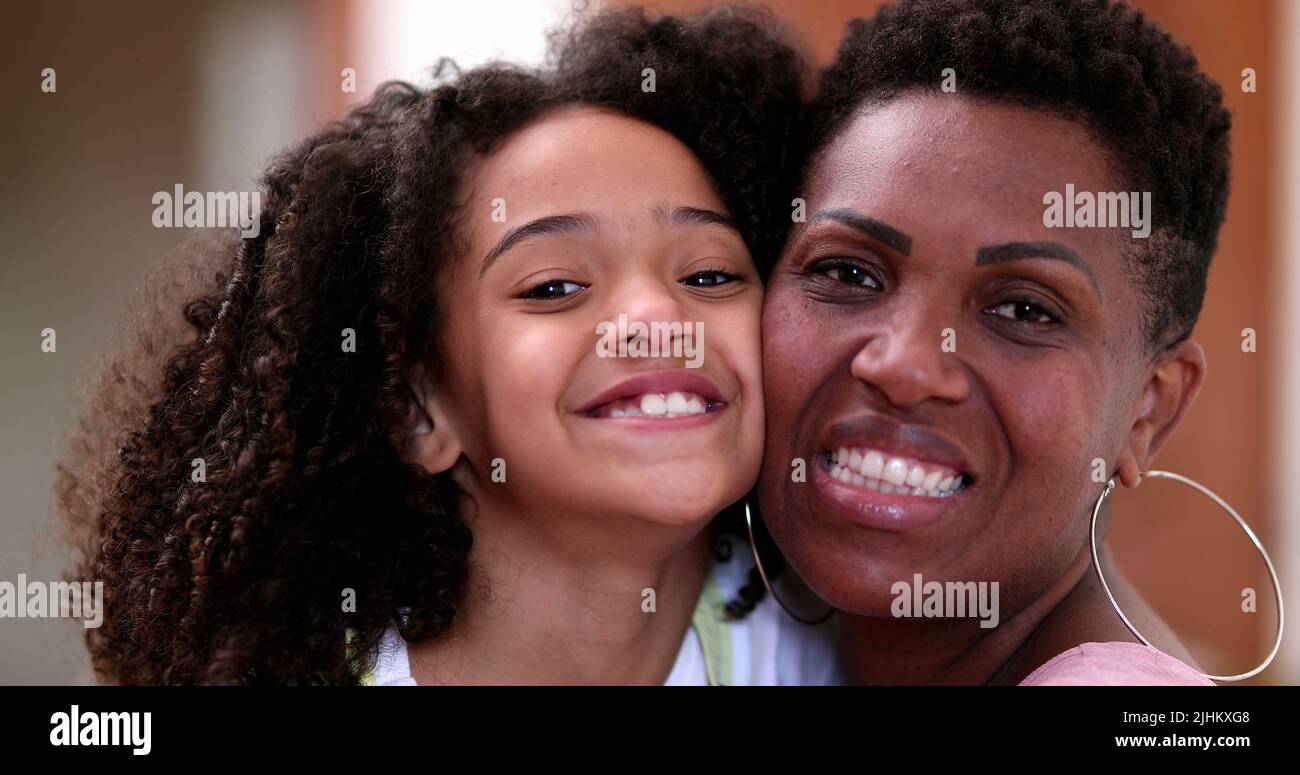 Happy African mother and daughter posing to camera smiling, cheek to ...