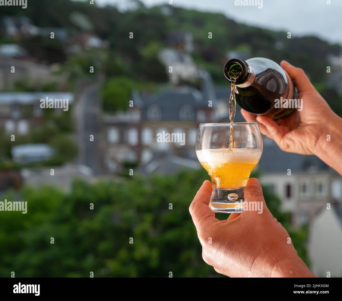 Pouring of tasty apple cider drink in glass with houses of Etretat ...