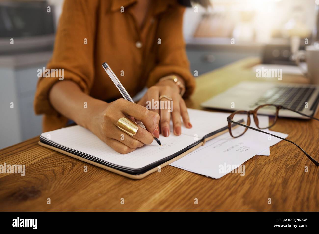 Mixed race businesswoman writing in a notebook while working from home ...