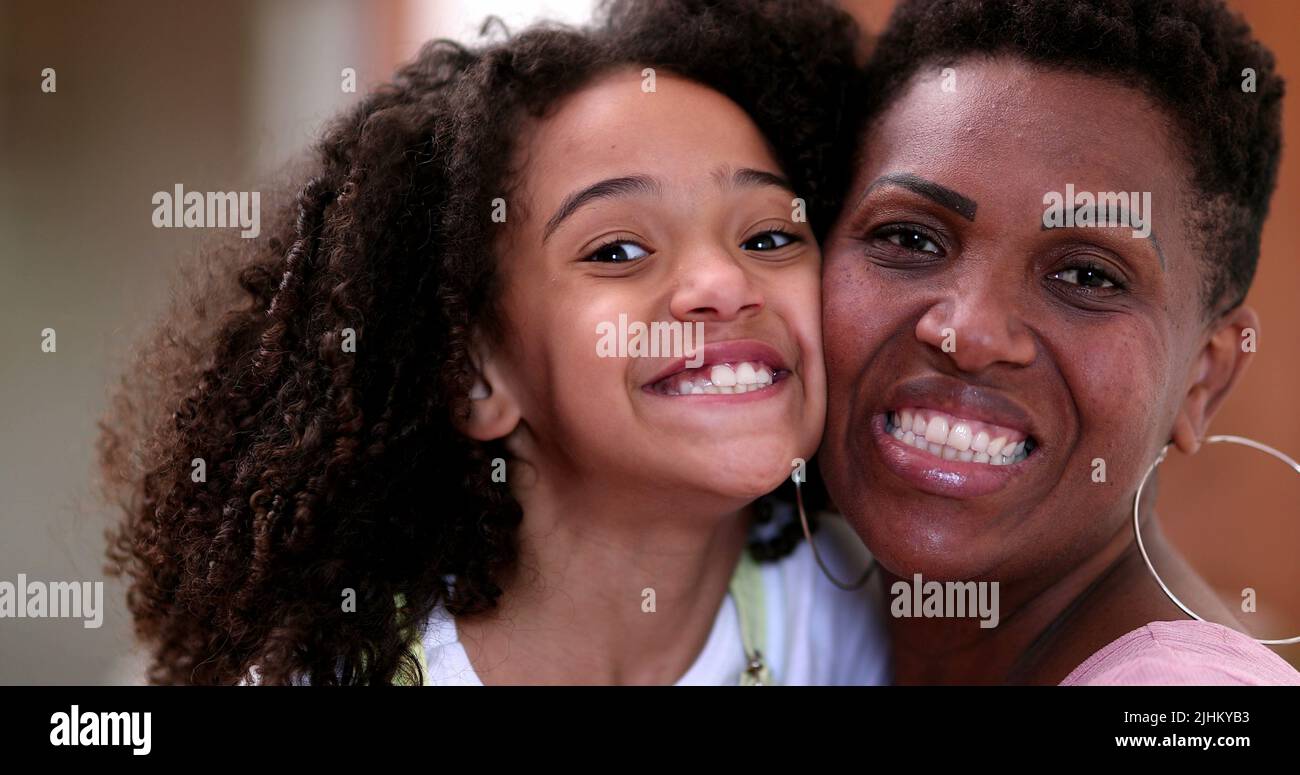 Happy African mother and daughter posing to camera smiling, cheek to ...