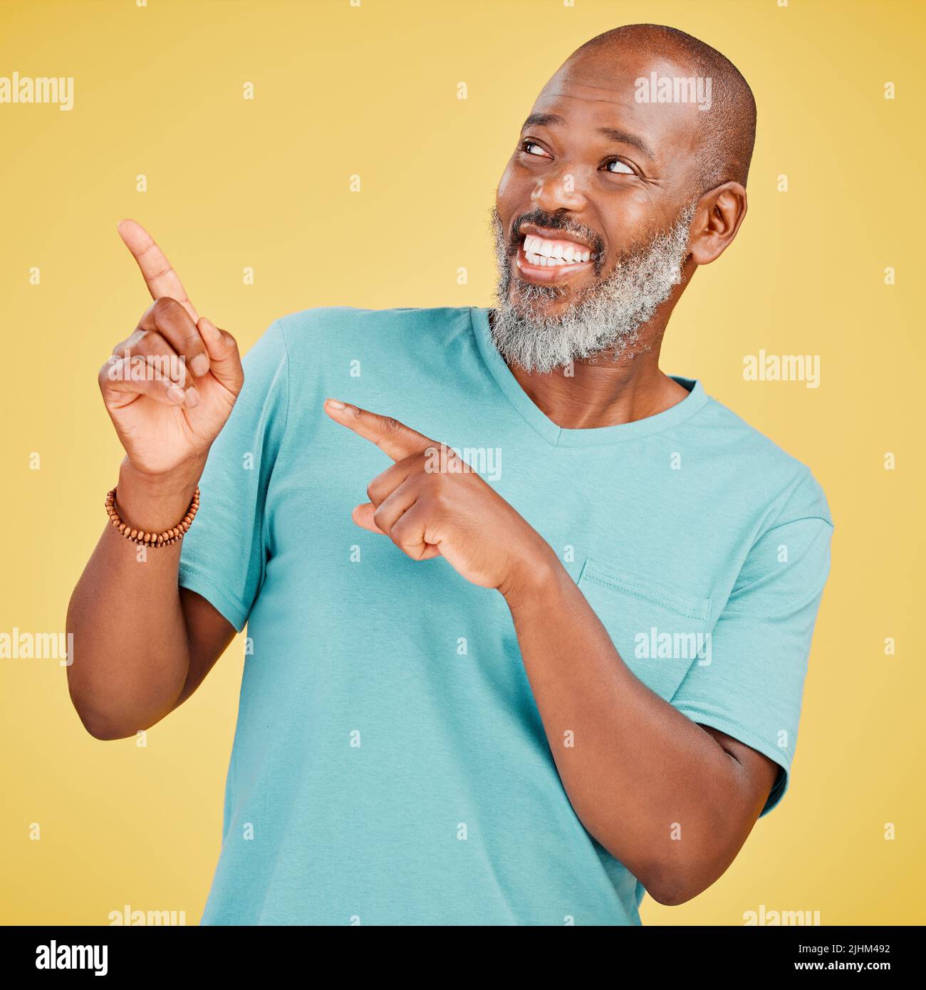 Mature african man smiling and pointing in a direction against a yellow ...