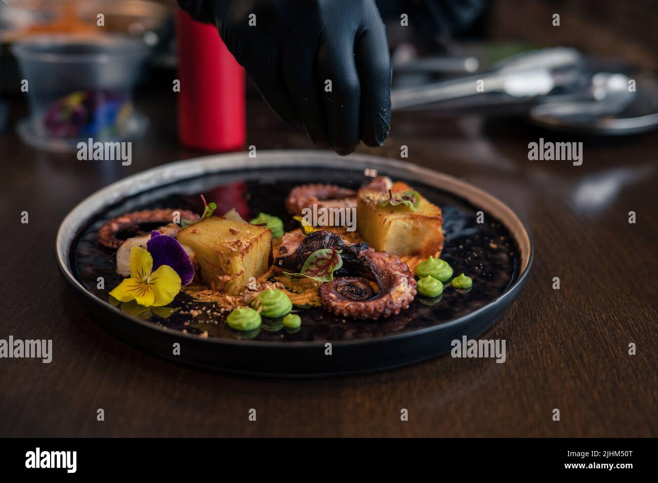 Chef preparing octopus with potatoes on pea mash decorated with edible ...