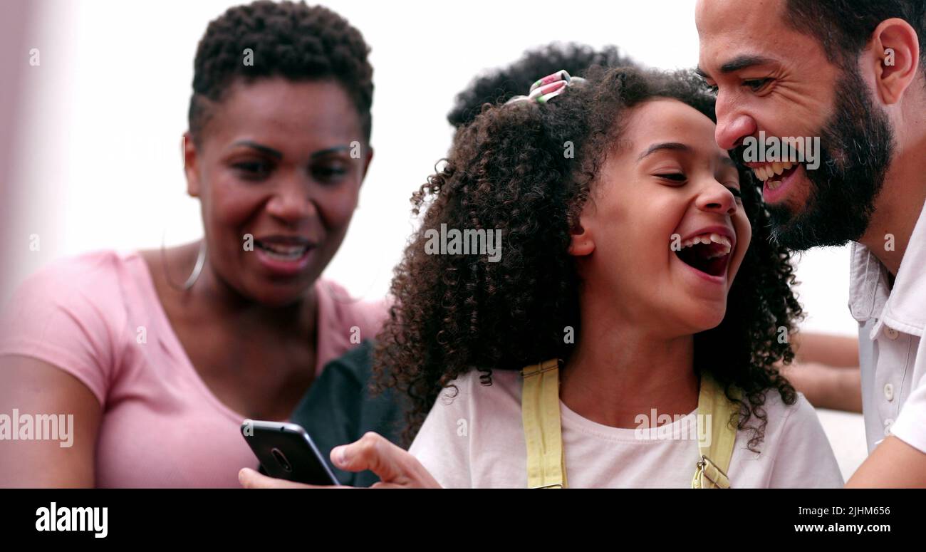 Happy multiracial family laughing and smiling together looking at phone ...