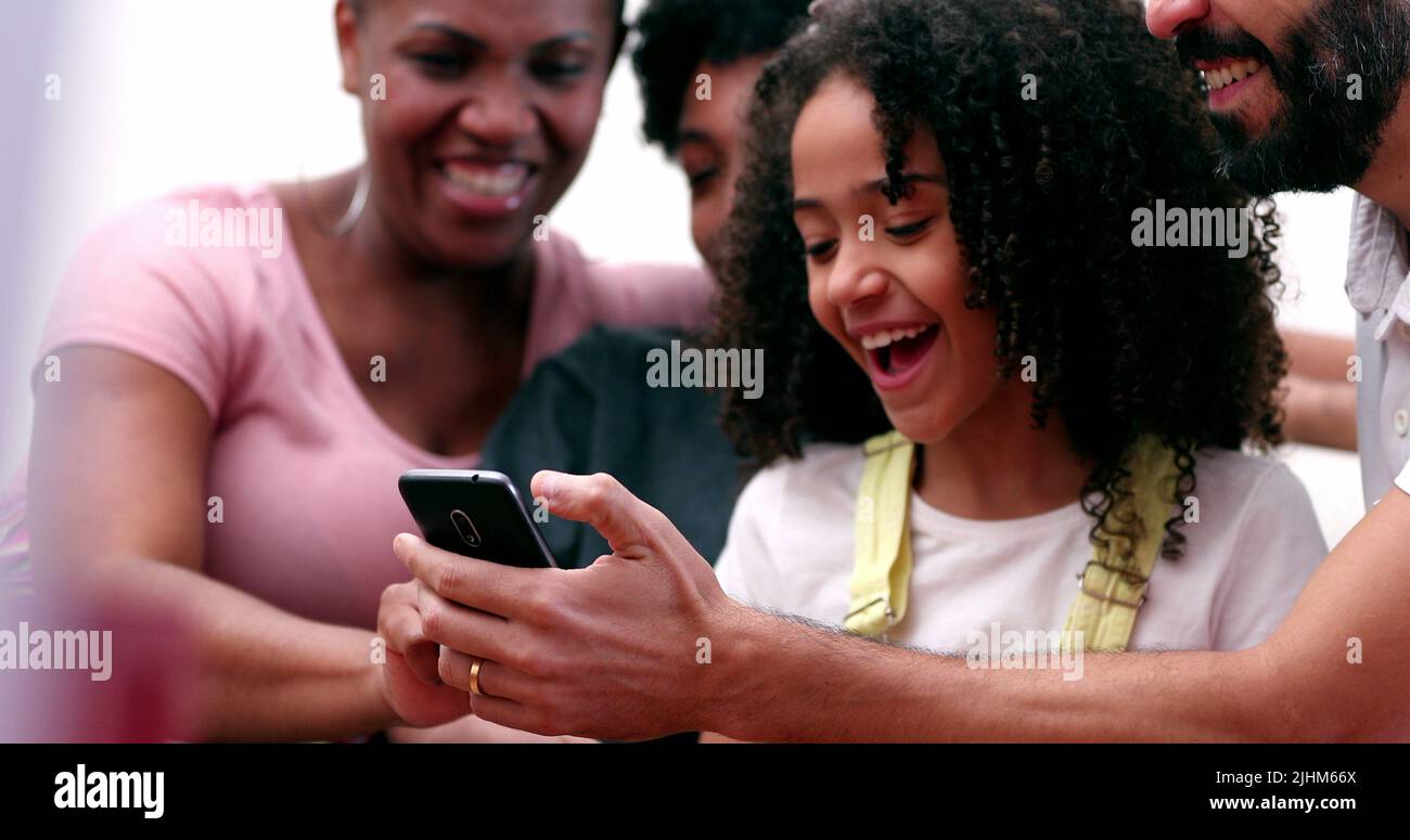 Happy multiracial family laughing and smiling together looking at phone ...
