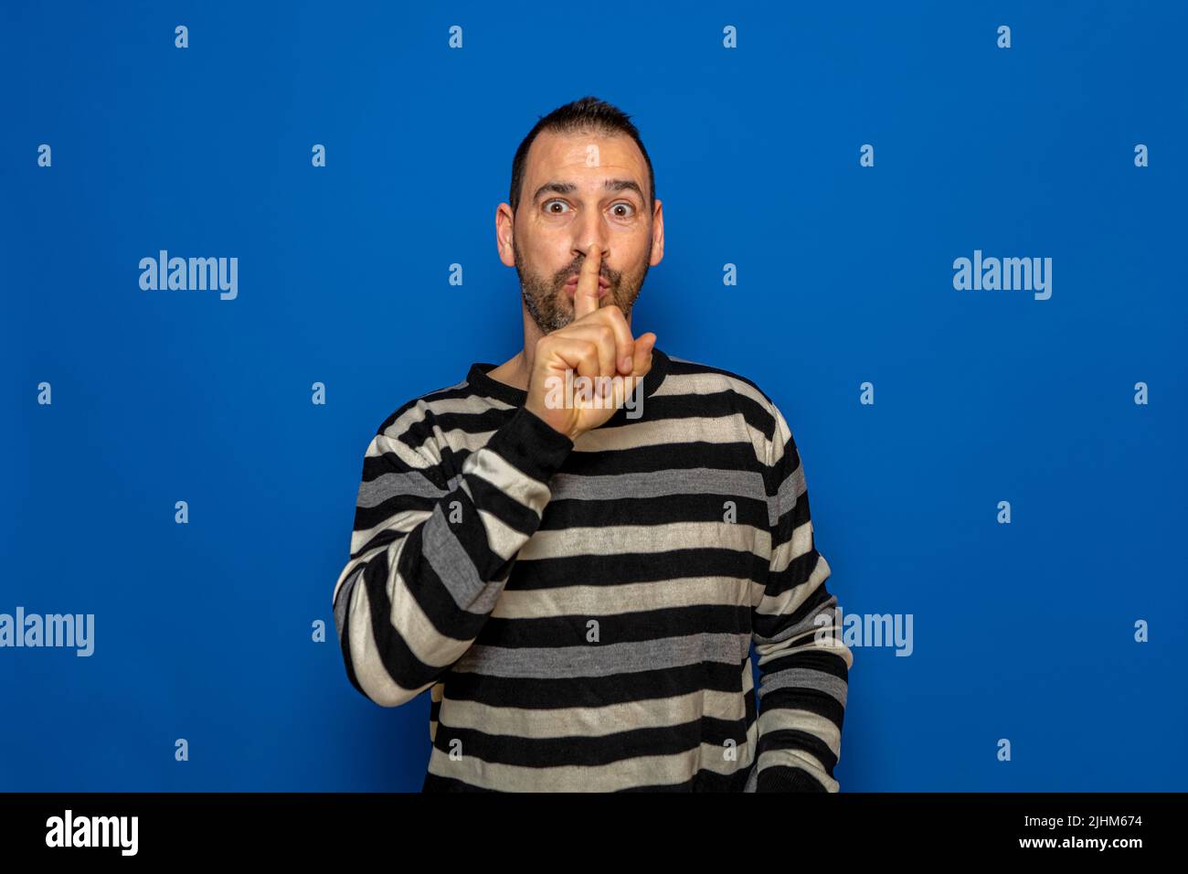 Positive smiling man with beard holding finger near lips showing shh ...