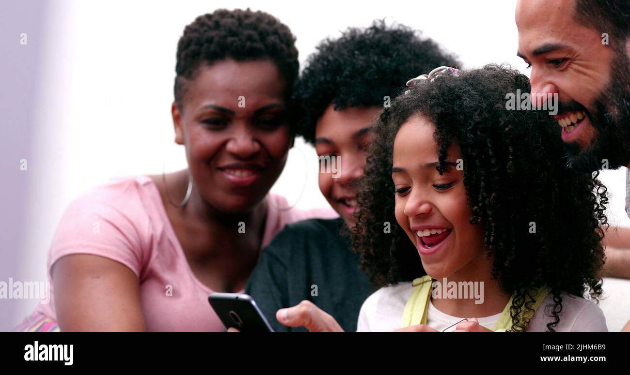 Happy multiracial family laughing and smiling together looking at phone ...