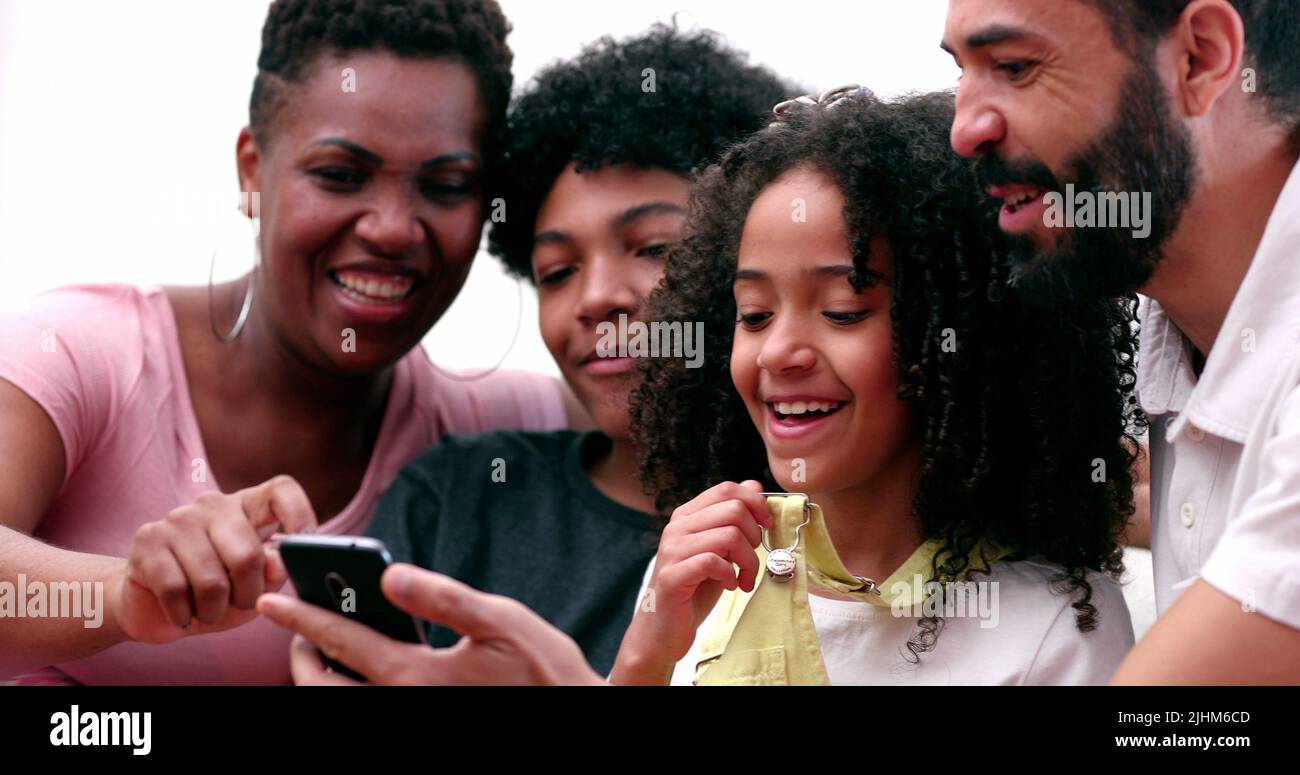 Happy multiracial family laughing and smiling together looking at phone ...