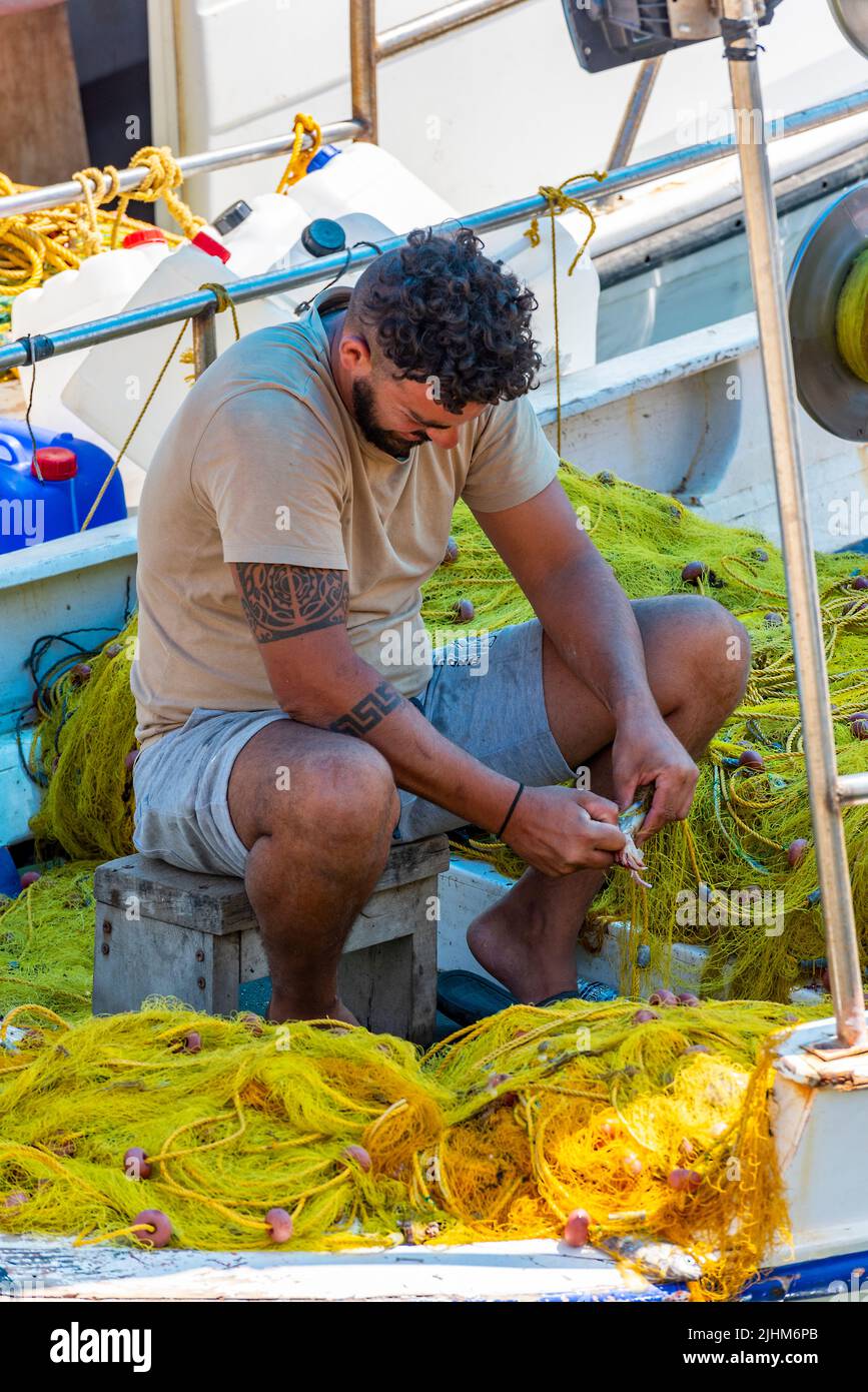 greek fisherman on the island of crete mending nets on his boat in a ...
