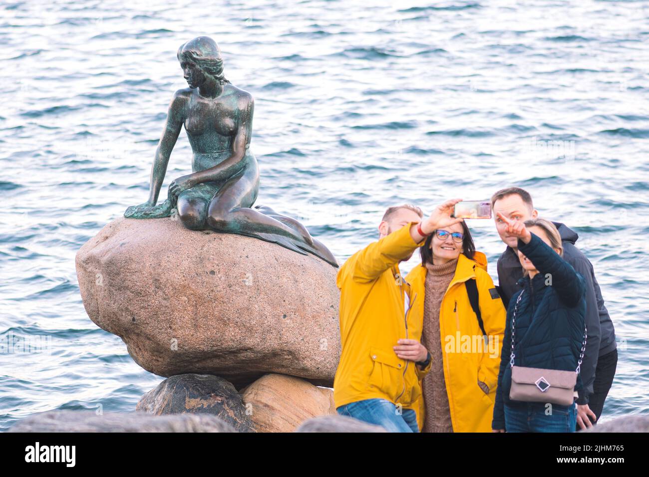 Bronze statue or sculpture of The Little Mermaid displayed on a rock by the waterside at the ...