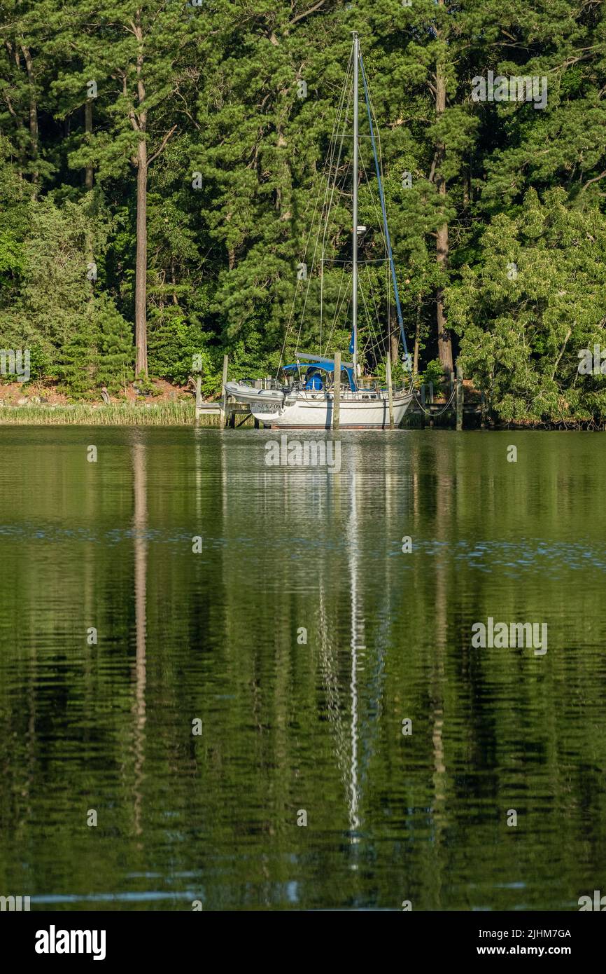 A sailboat docked on a shore lined with trees Stock Photo - Alamy