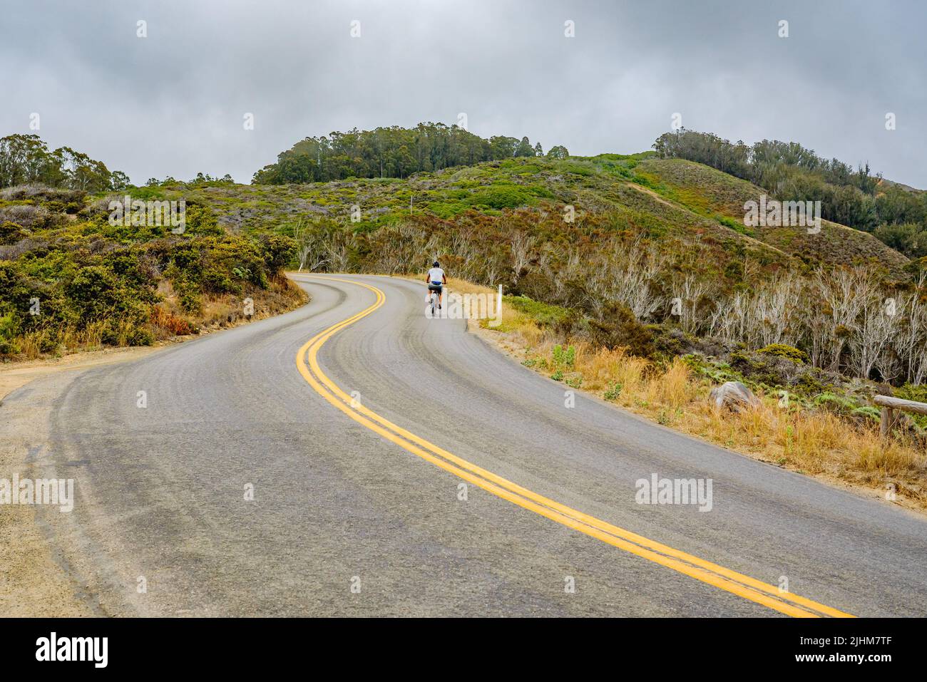 Curving asphalt road with yellow lines, and silhouette of bicyclist ...