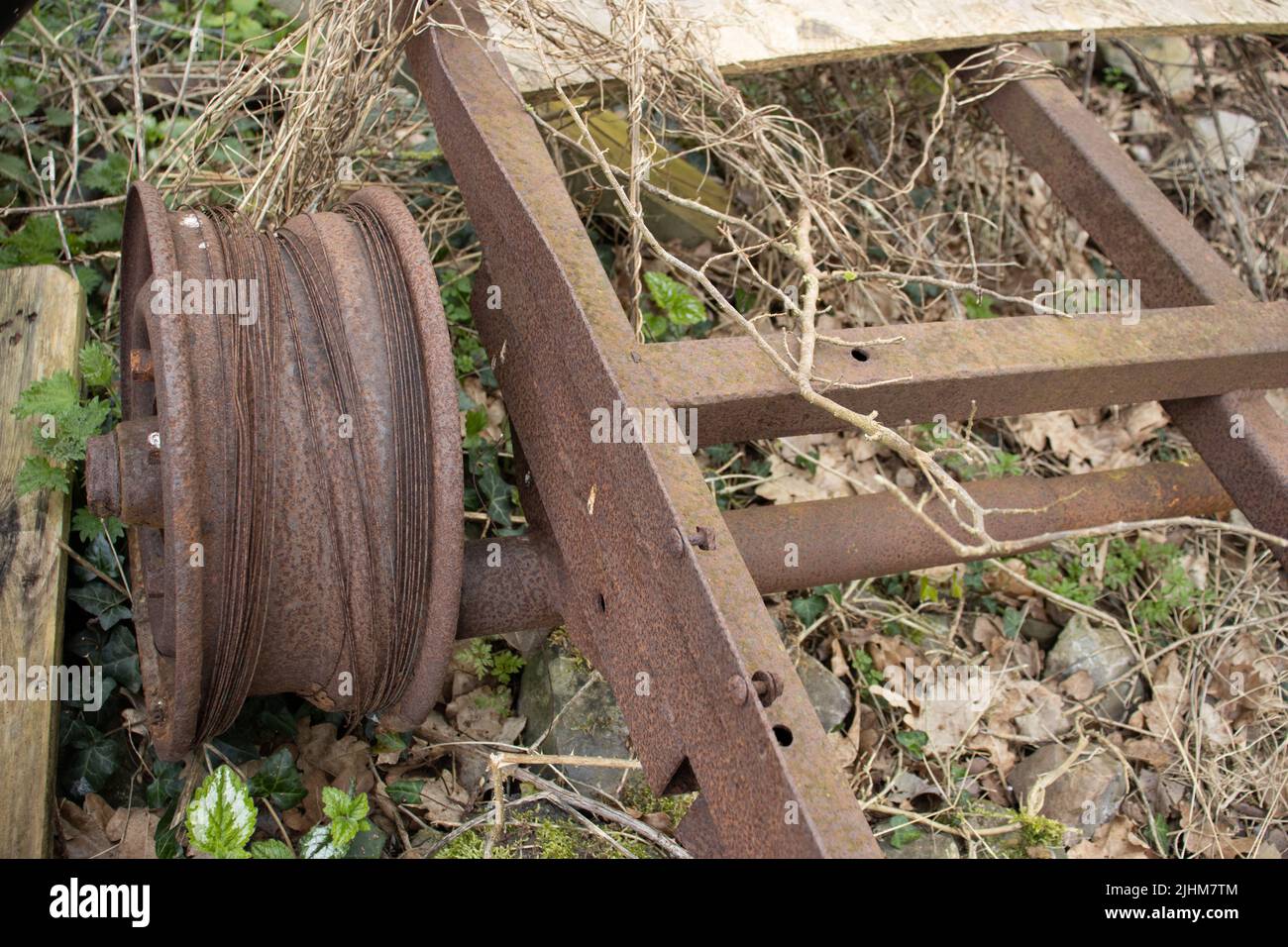 pile of rusting and broken farm trailer and wheel with grass and weeds ...