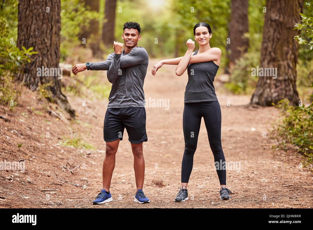Portrait of a happy young male and female athlete stretching their arms ...