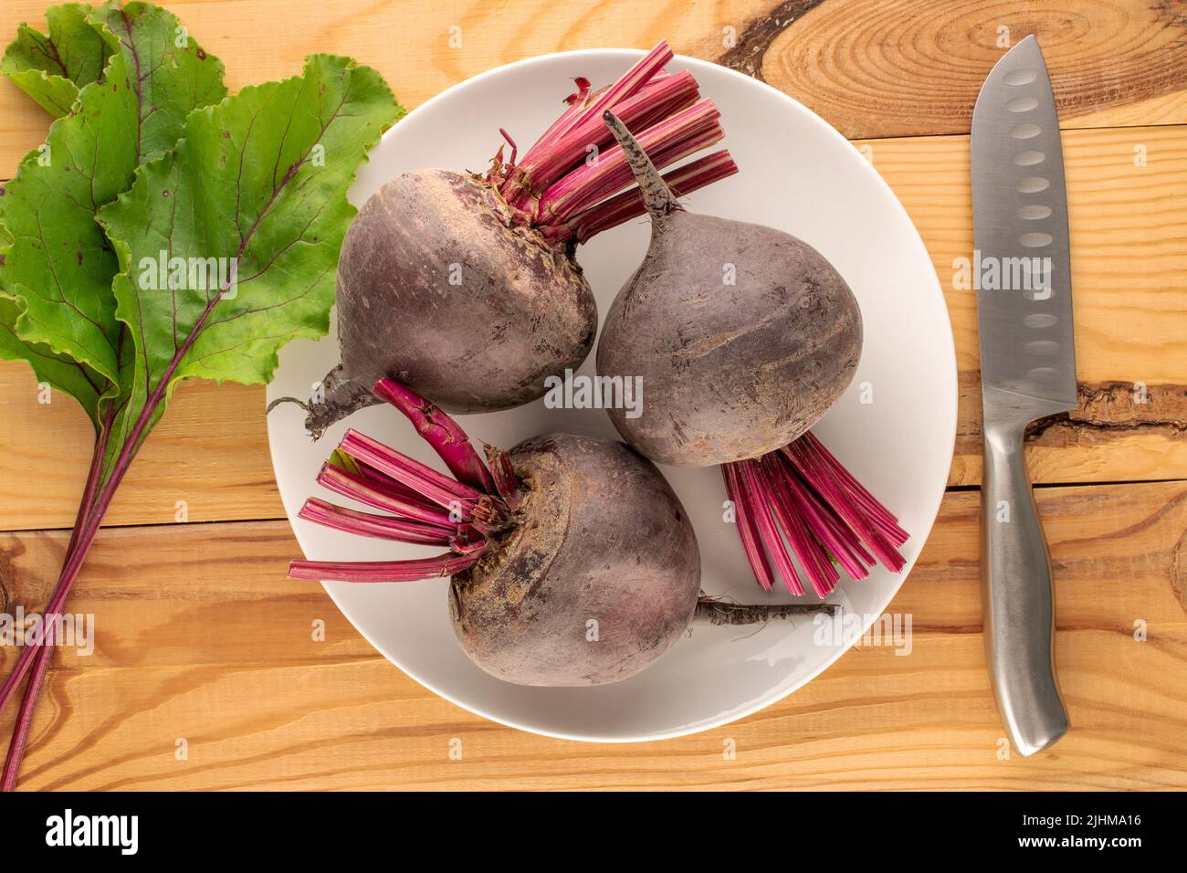 Three sweet red beets with ceramic plate and metal knife on wooden ...