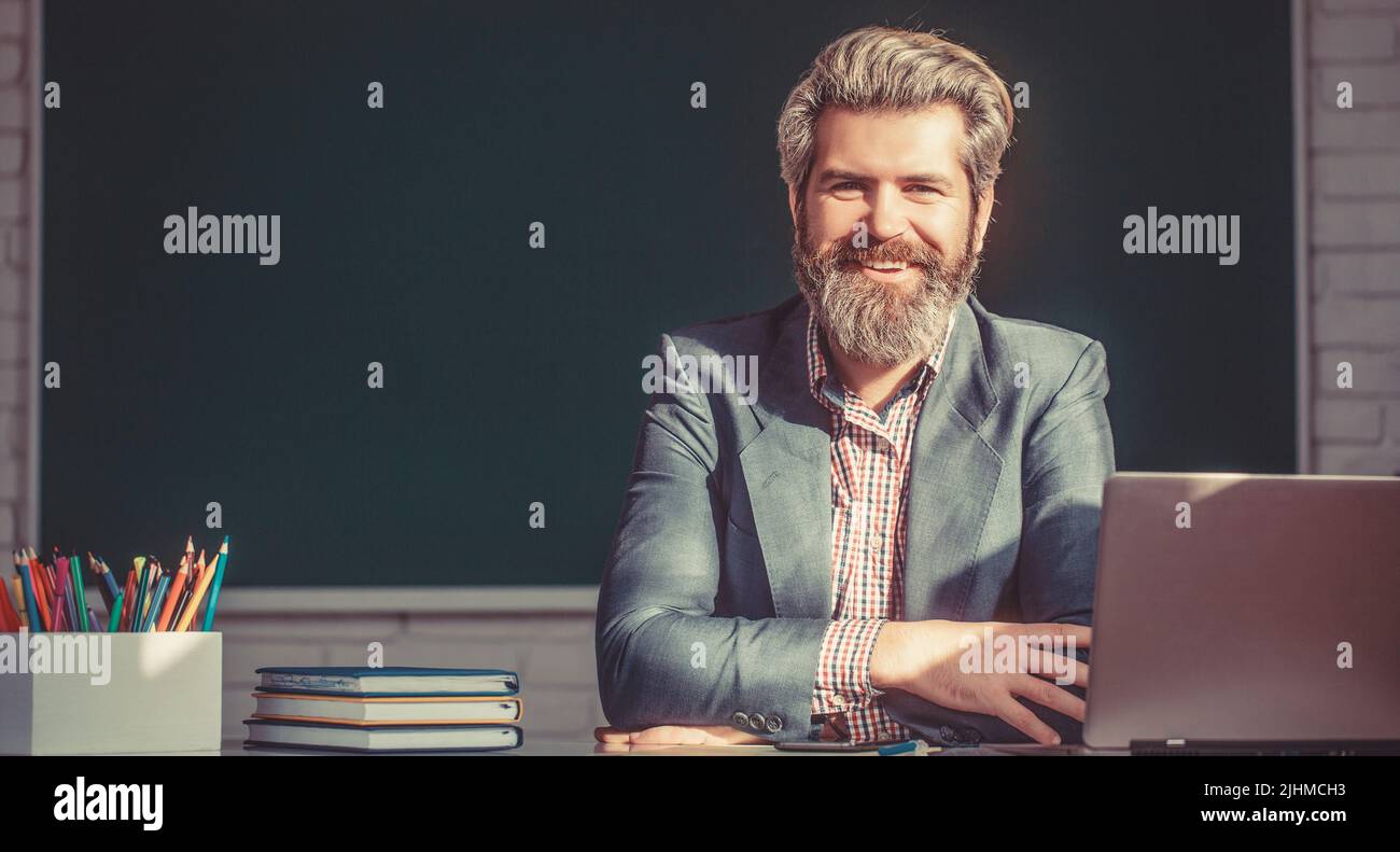 male teacher with laptop in class sits at the table the blackboard in ...