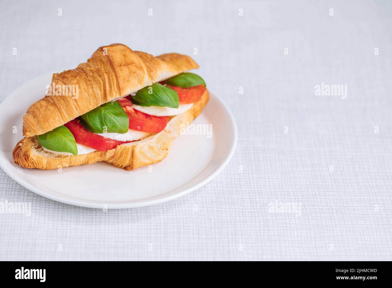 Croissant sandwich with basil, tomato and mozzarella cheese on white ...