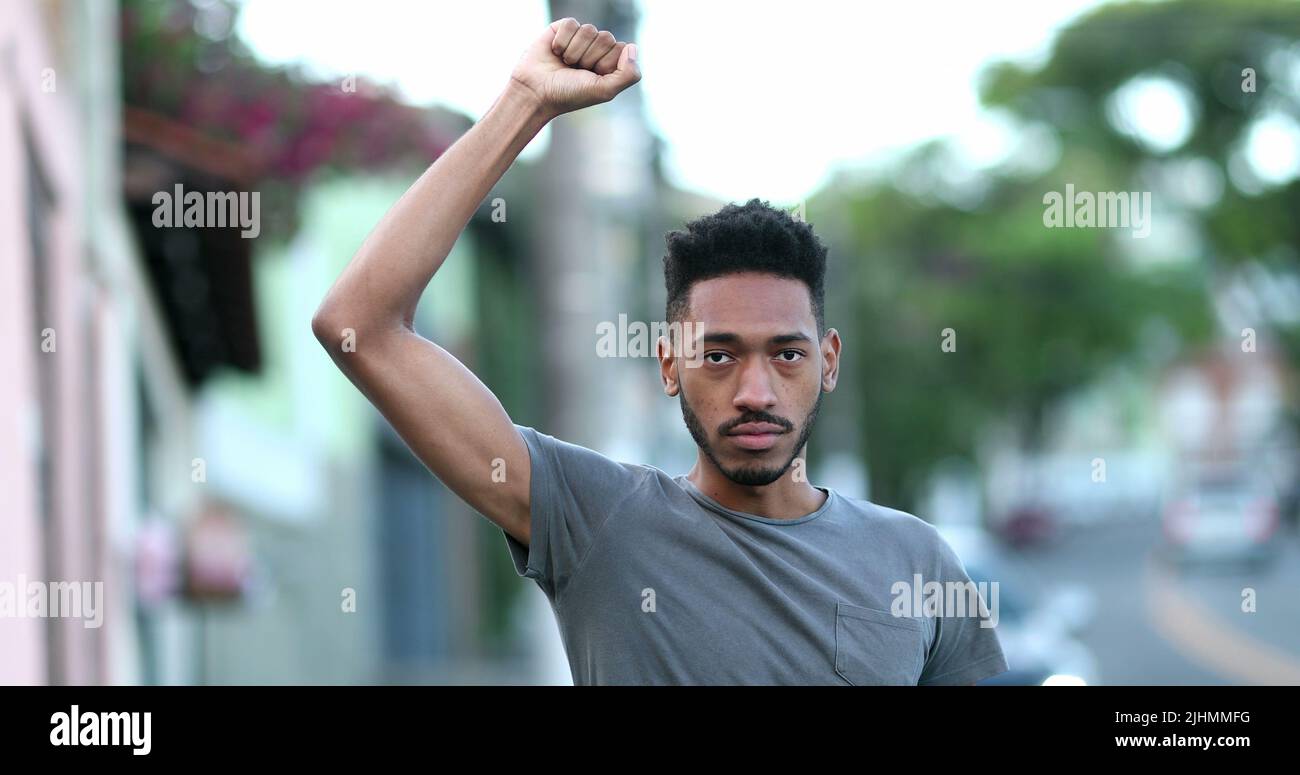 Individual young black man raising fist in air staring camera in ...