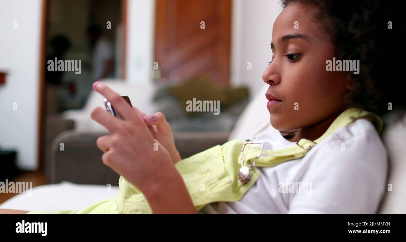 Little black girl using smartphone device at home sofa. African ...