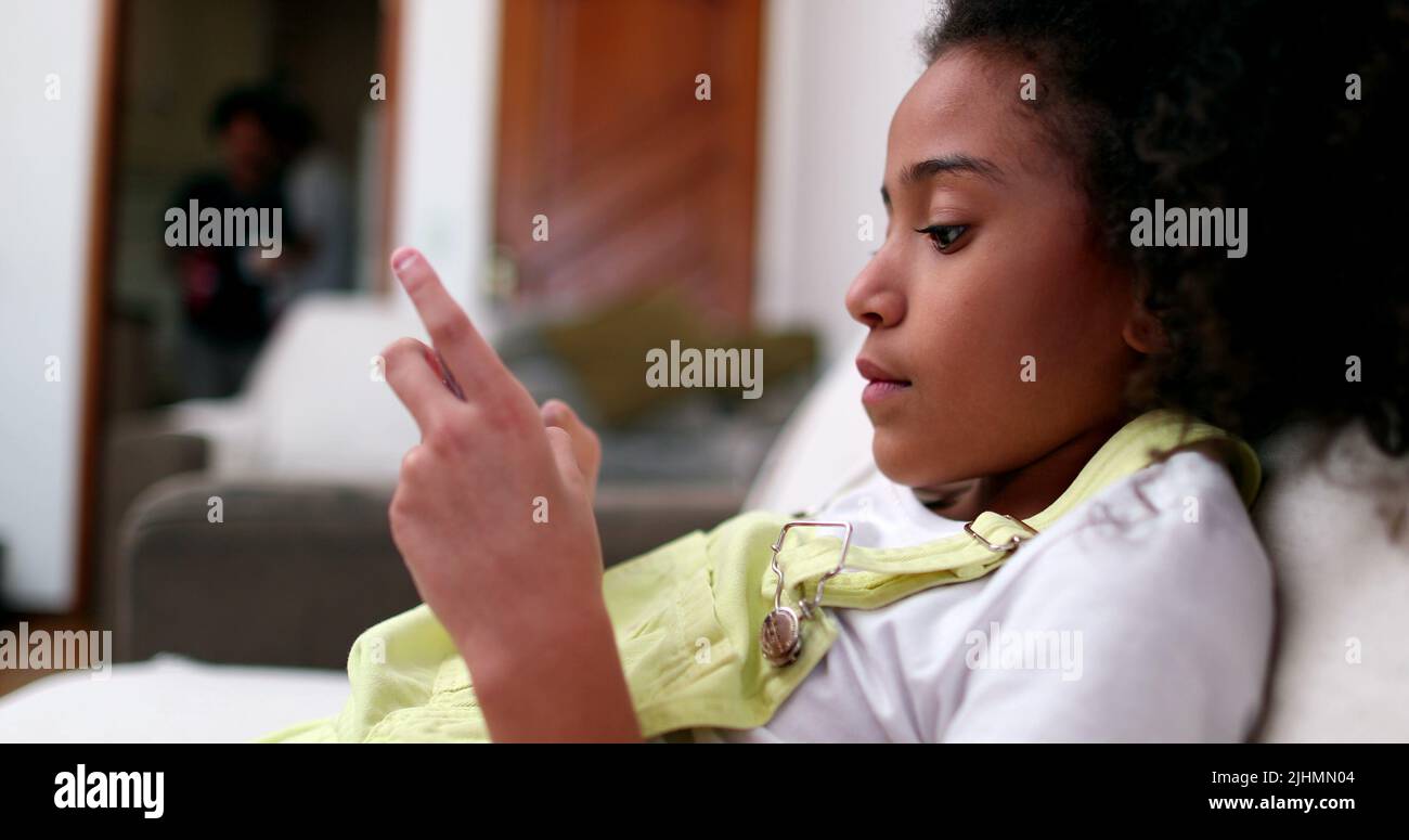 Little black girl using smartphone device at home sofa. African ...