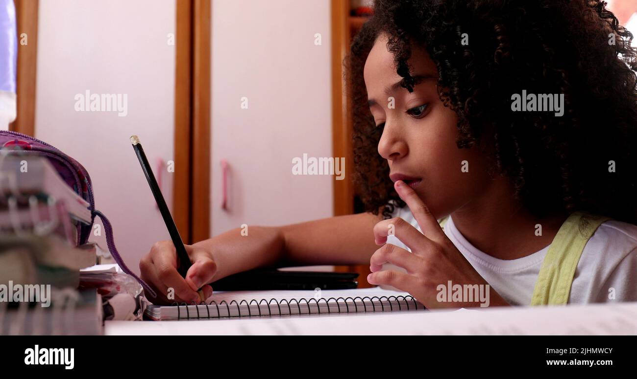 Little girl studying at home, mixed race child writing notes doing ...