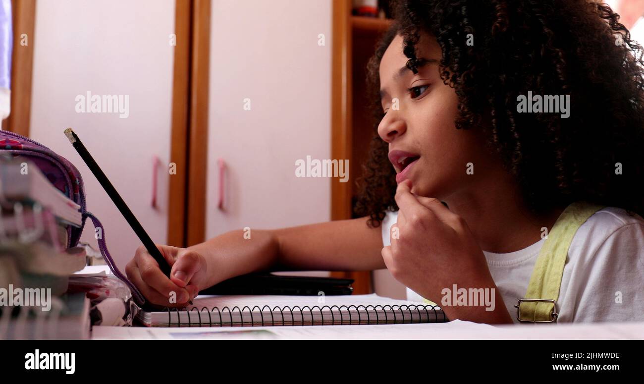 Little girl studying at home, mixed race child writing notes doing ...